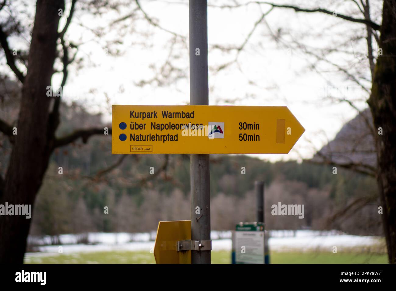 A yellow directional sign with an arrow pointing left, standing upright ...
