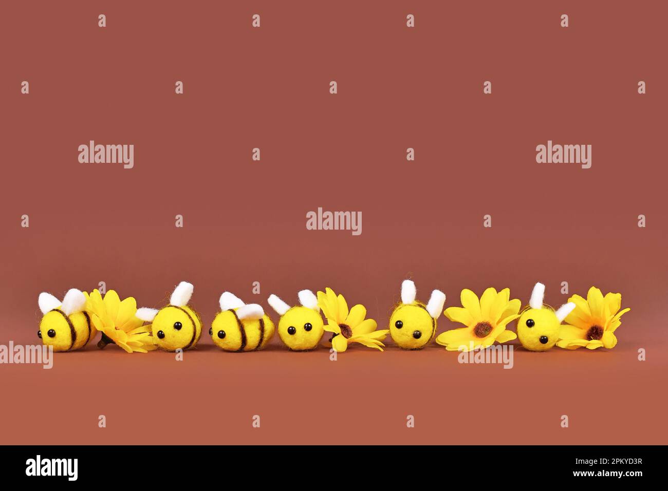 Felt bees and yellow flowers in a row on brown background with copy ...