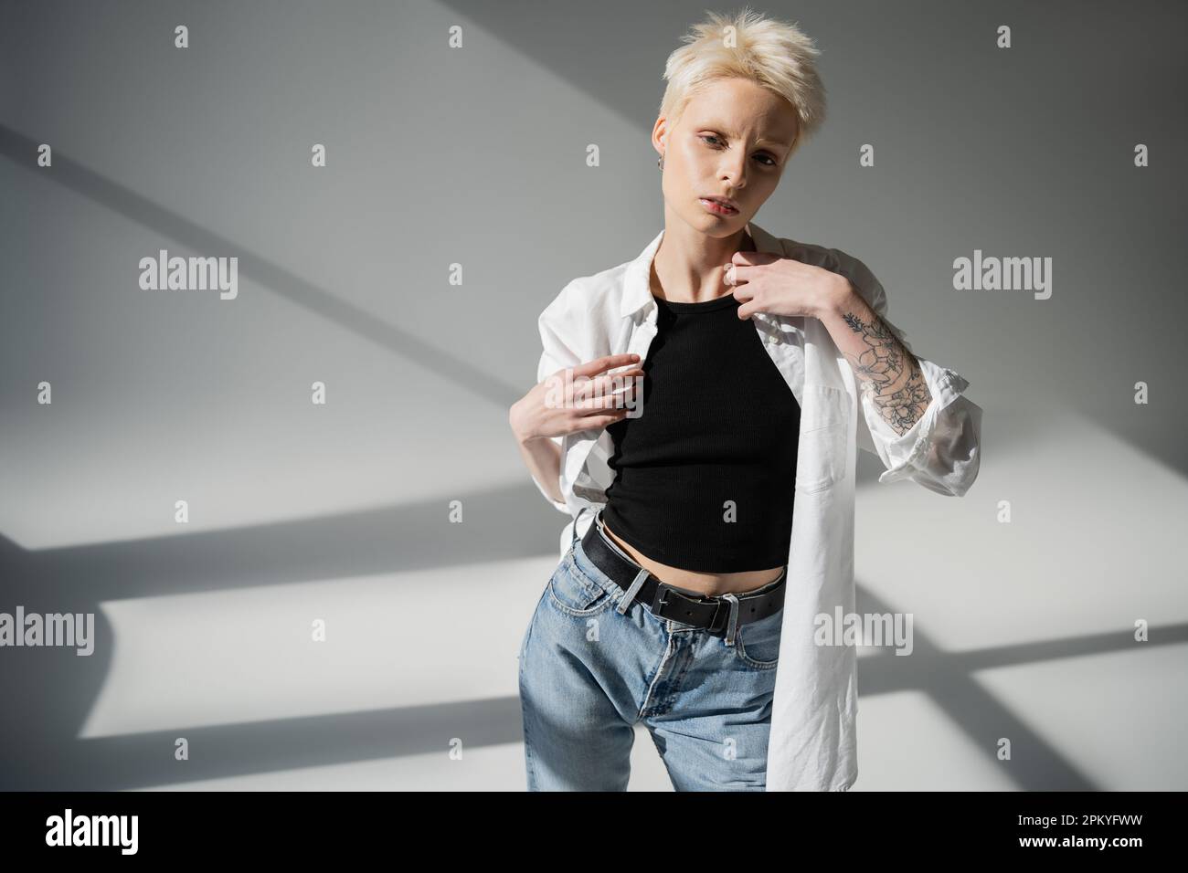 young albino woman with tattoo on hand wearing white shirt on grey ...