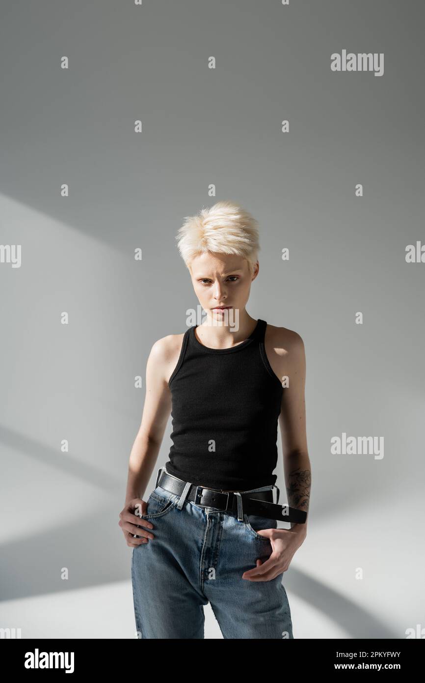 serious albino woman with tattoo on hand posing in jeans and tank top ...