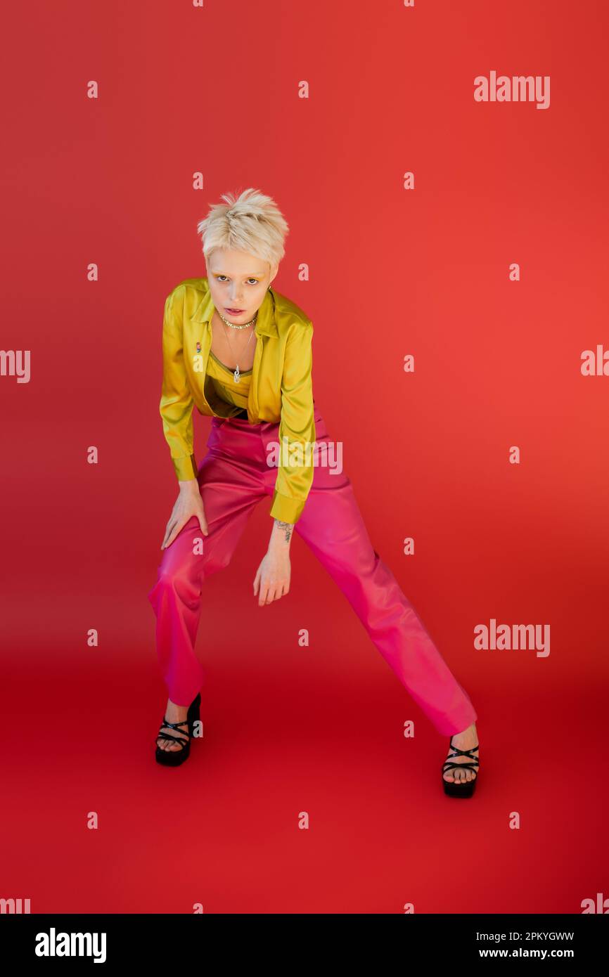 full length of young albino model in trendy outfit posing on carmine ...