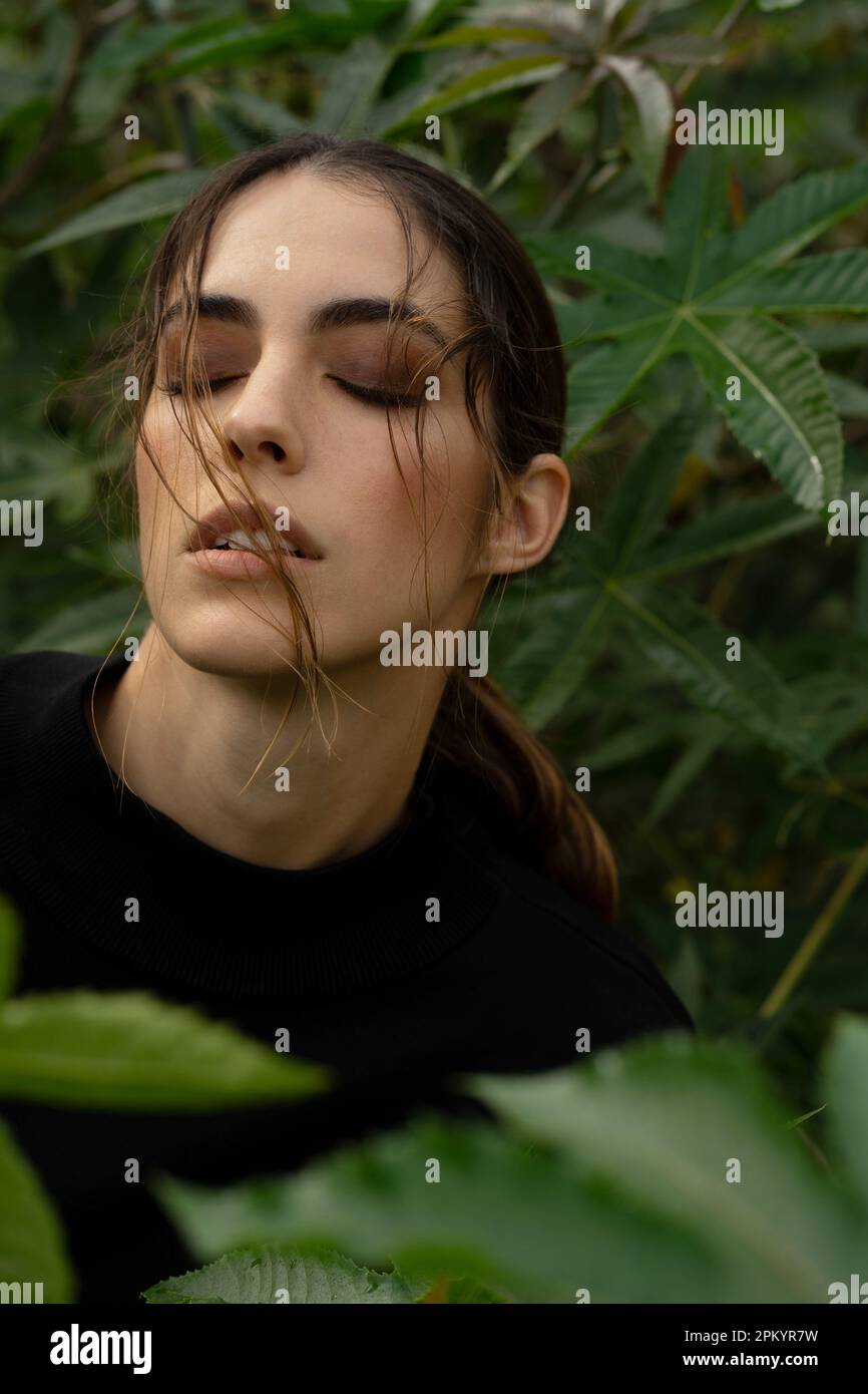 Calm young female model in black outfit with makeup and closed eyes ...