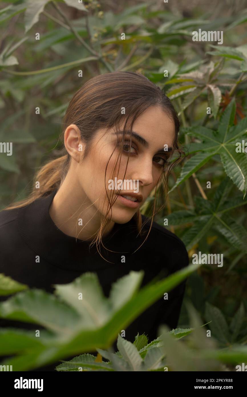 Calm young female model in black outfit with makeup standing looking at ...