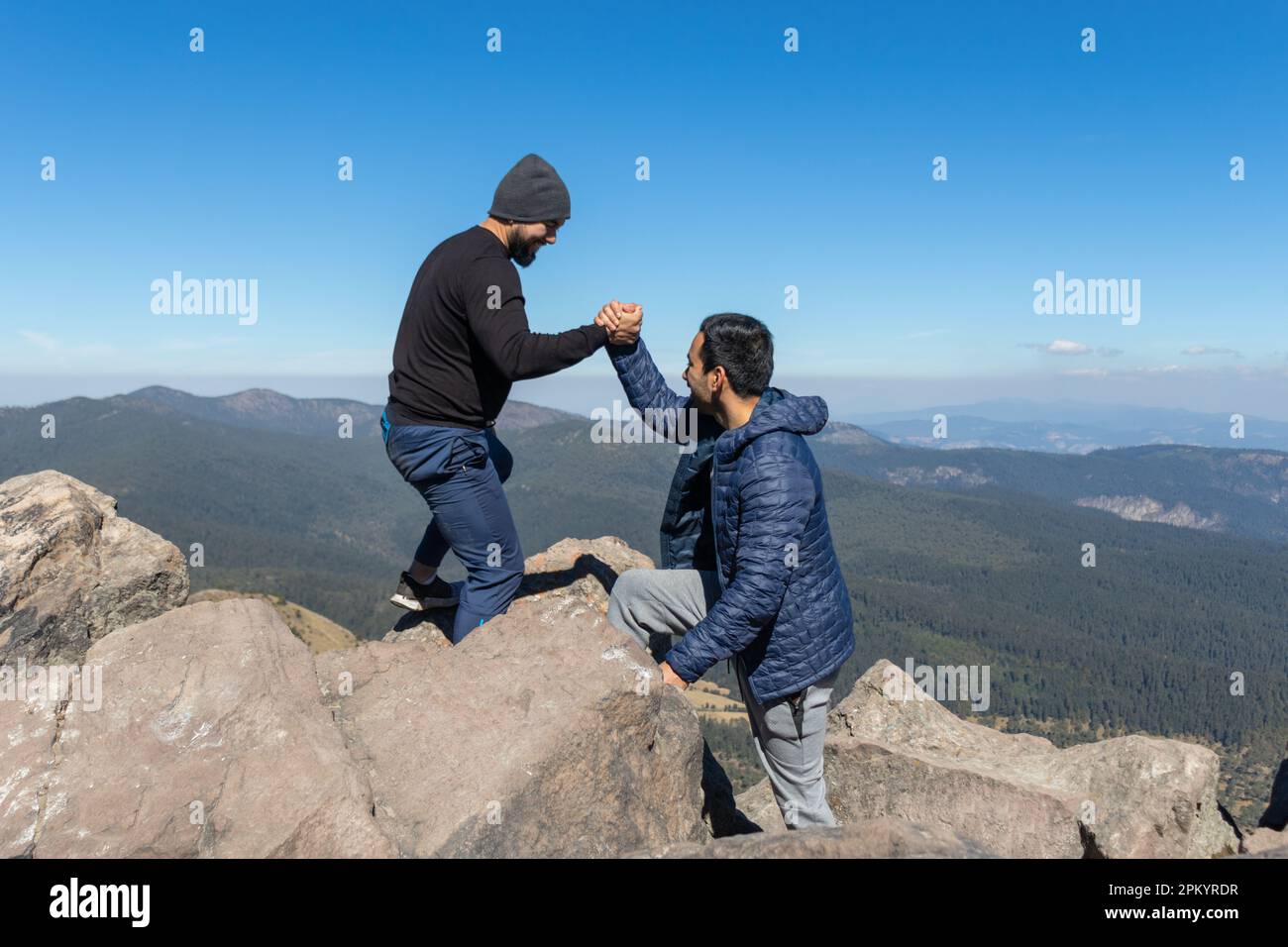 Cheerful bearded male hiker helping friend to climb on rocky Pico del ...