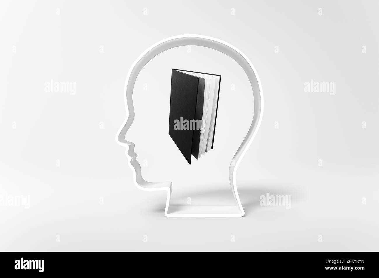 Black book with half open pages placed inside human head against white ...