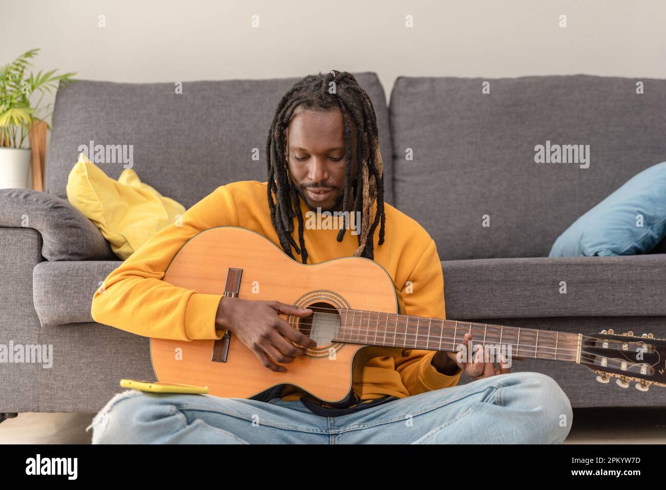 Happy African American male musician with dreadlocks sitting on floor ...