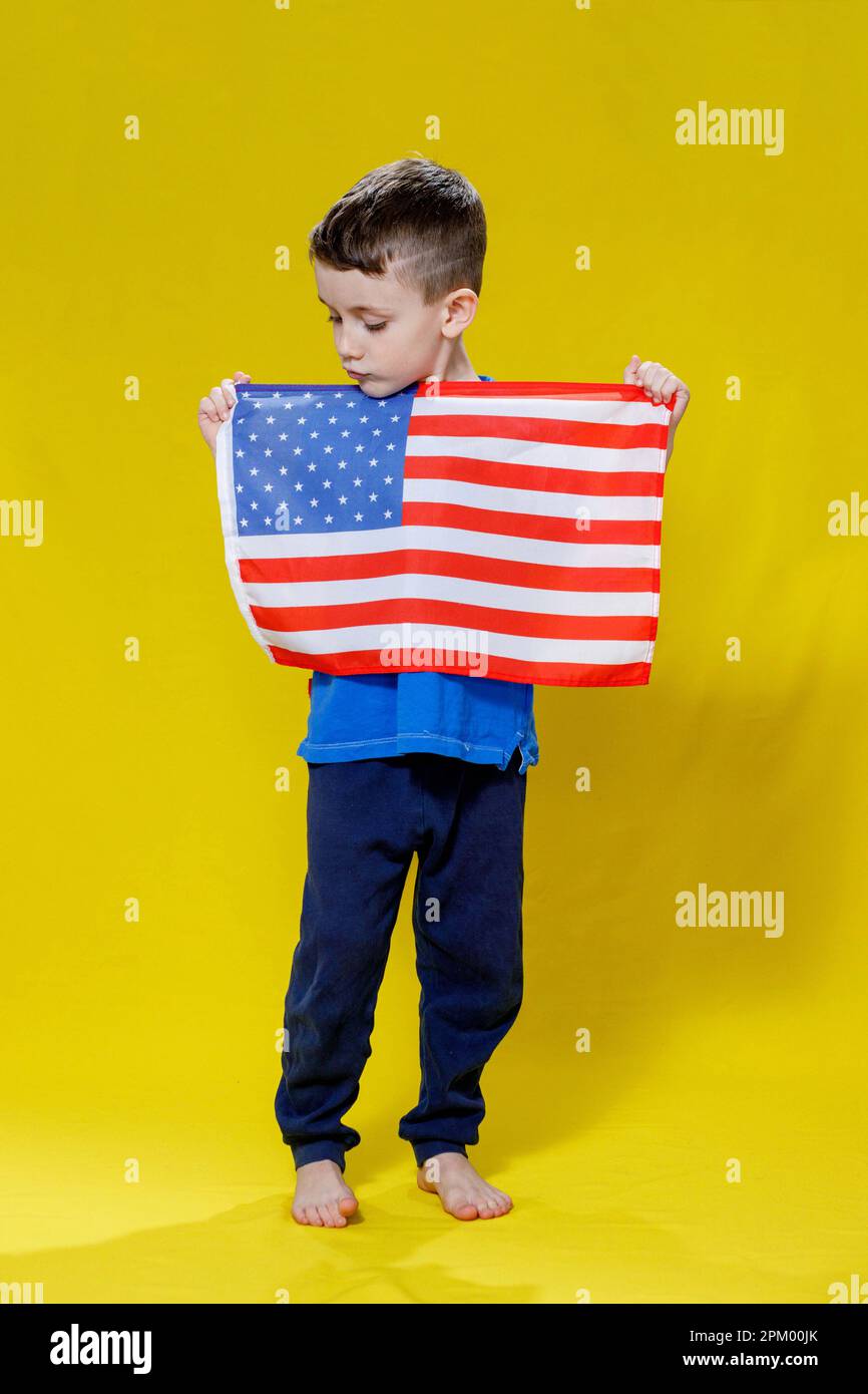 Little smiling boy holding an American flag on a yellow background ...