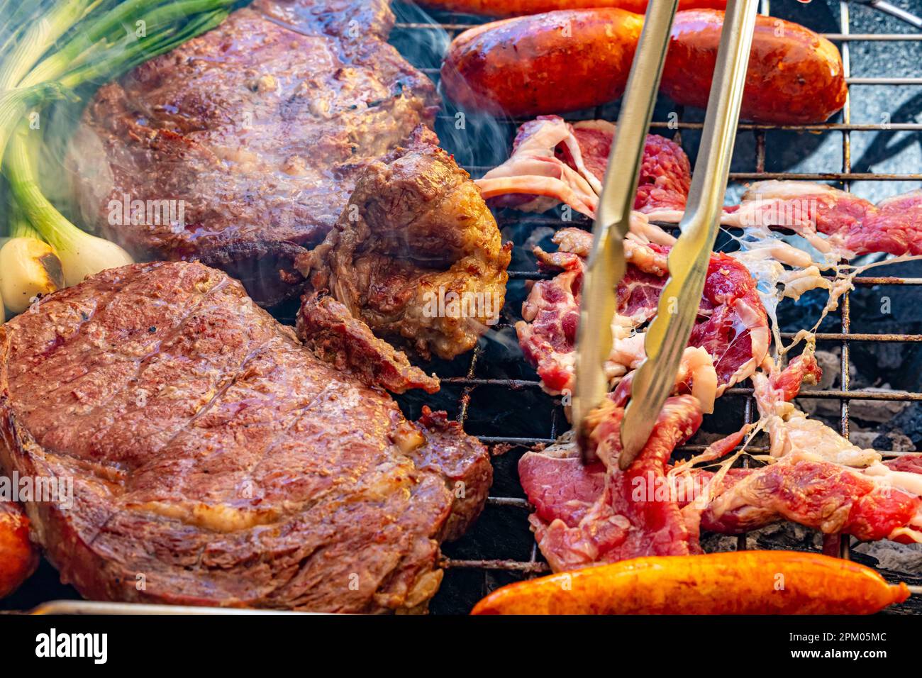 Close-up of beef steaks, chorizo and white onions grilling over ...