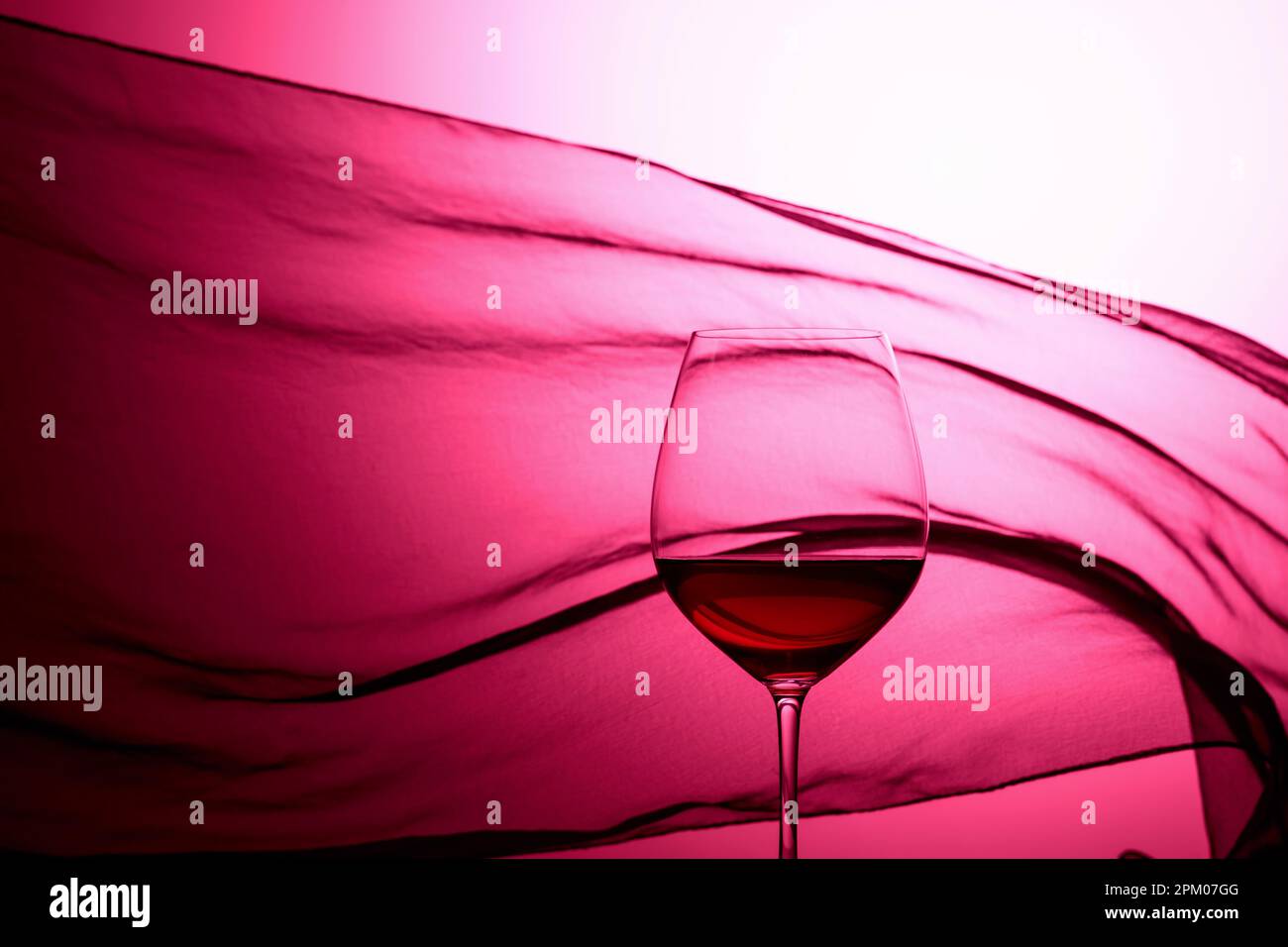 Glass of red wine on a background of waving satin curtain. Red backlit ...
