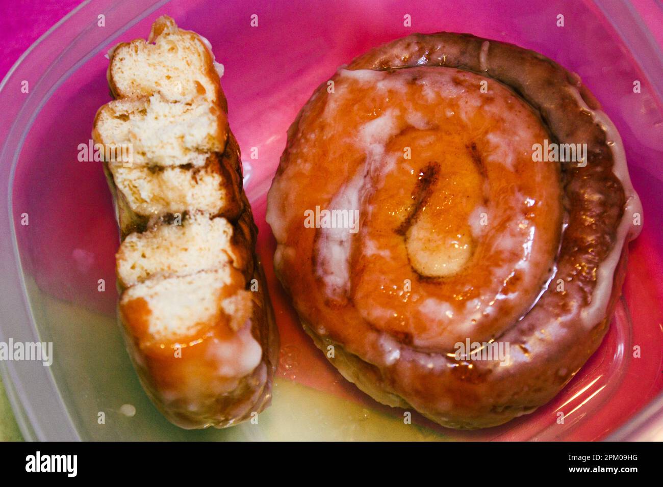 Honeybun covered in icing in clear container with bite taken out of it ...