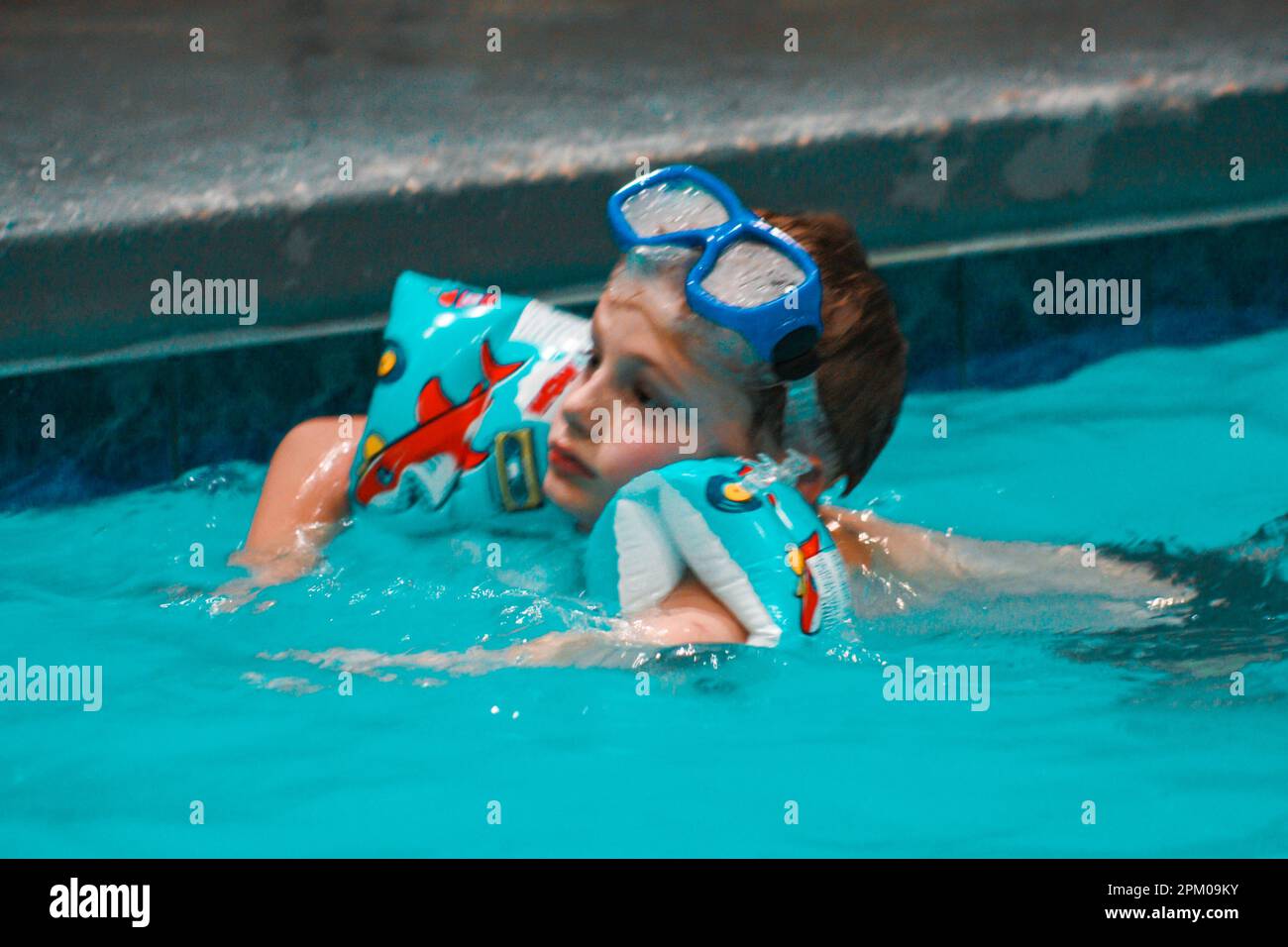Little boy playing in an indoor swimming pool wearing goggles and ...