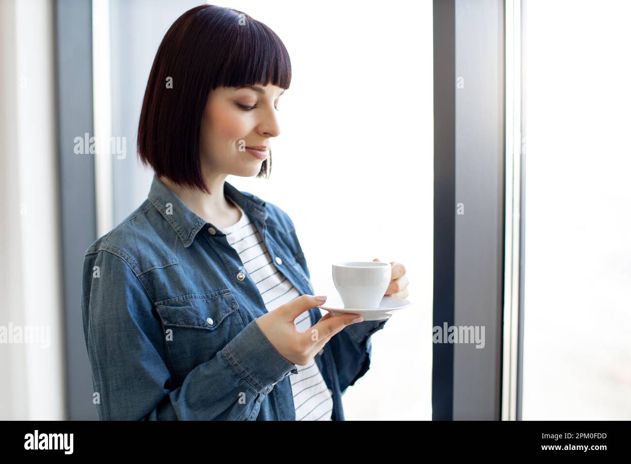 Side view of attractive young woman in casual wear holding white cup ...