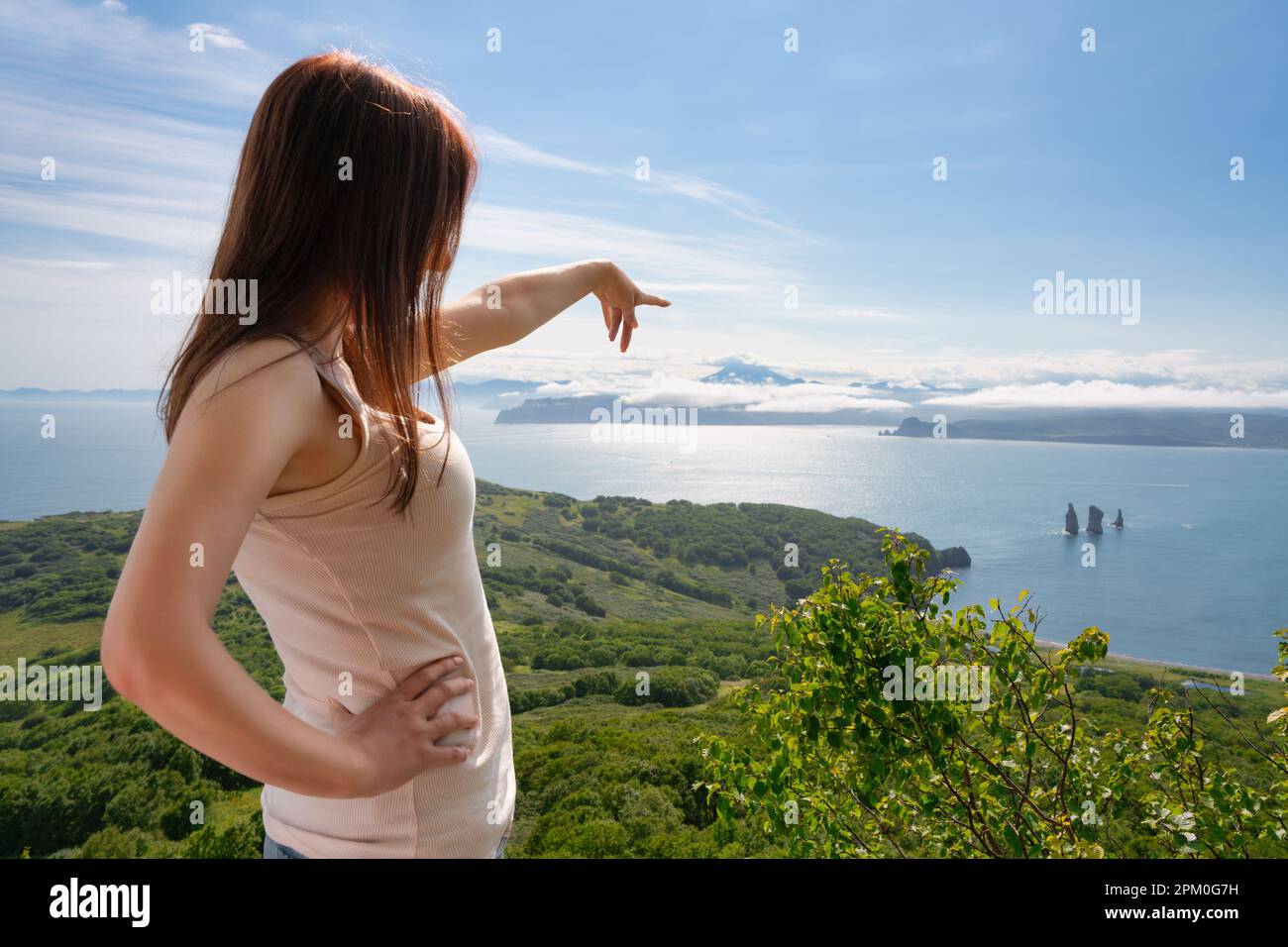 Faceless woman points with hand at blue sea below, standing high in ...