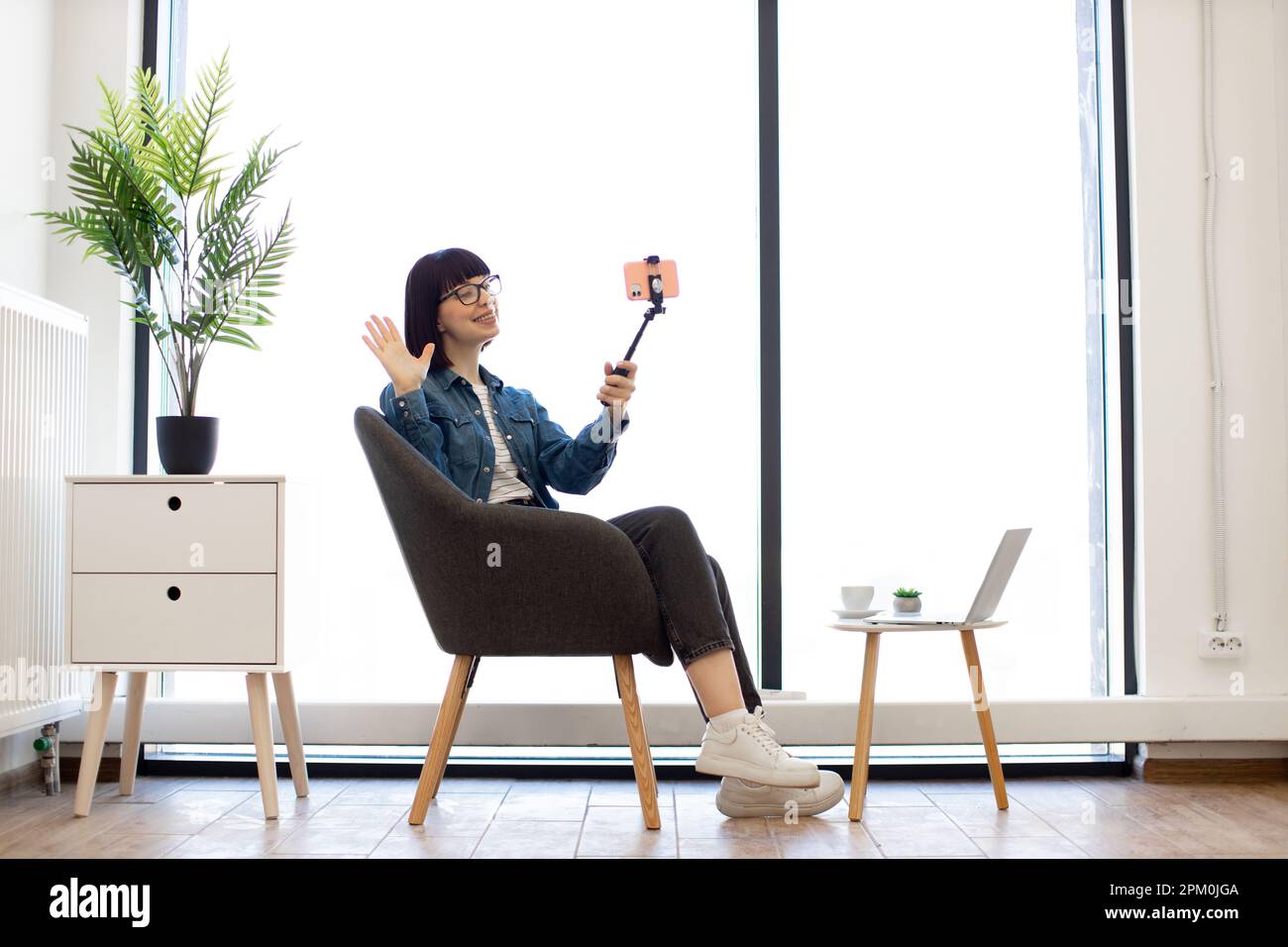 Cheerful woman in casual outfit holding stick with smartphone while ...