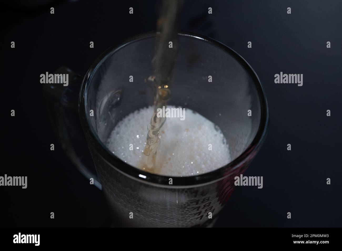 A stream of beer pours into a glass. Dark background Stock Photo - Alamy