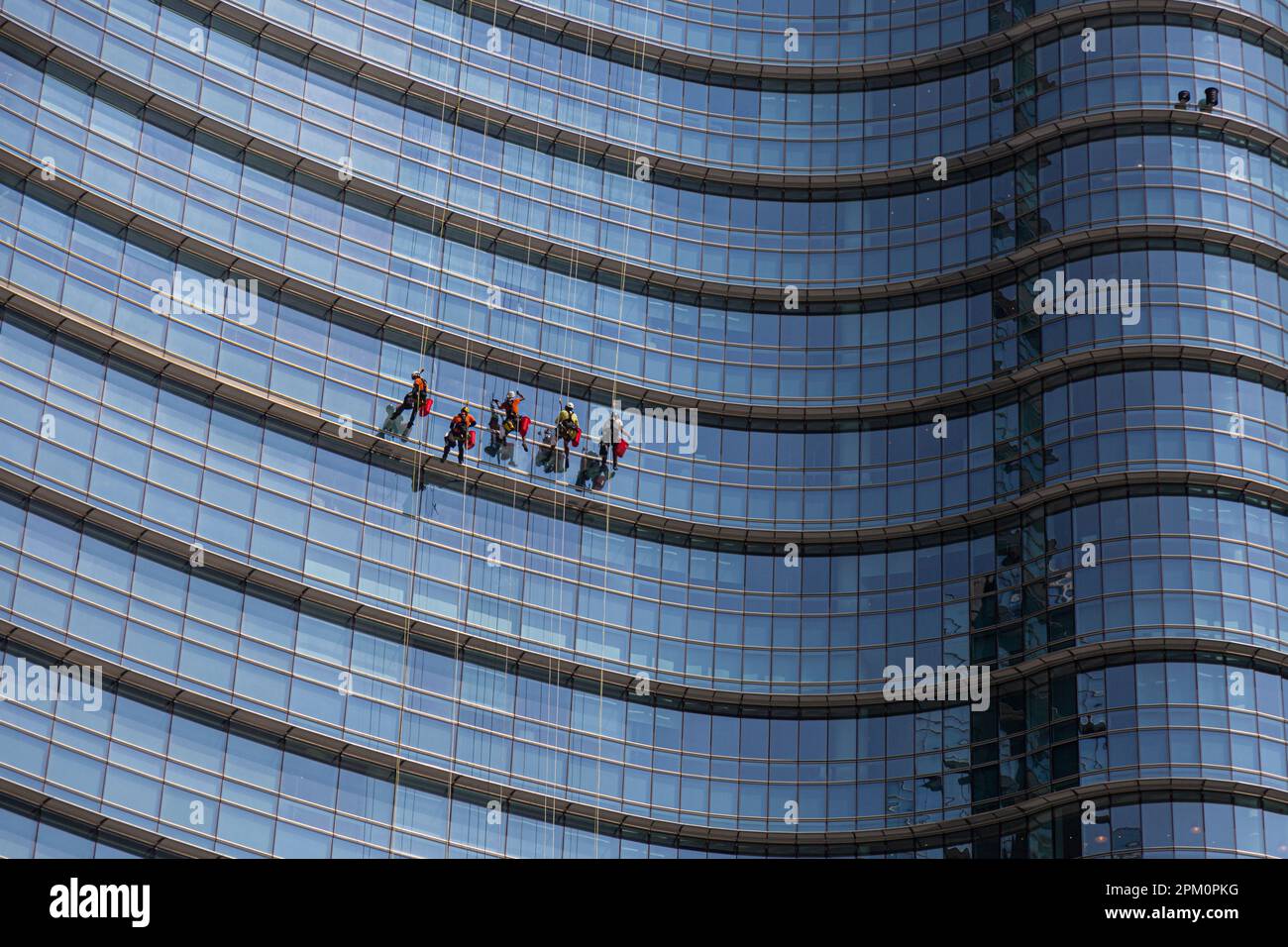 A glass building with window washers descending the facade on climbing ...