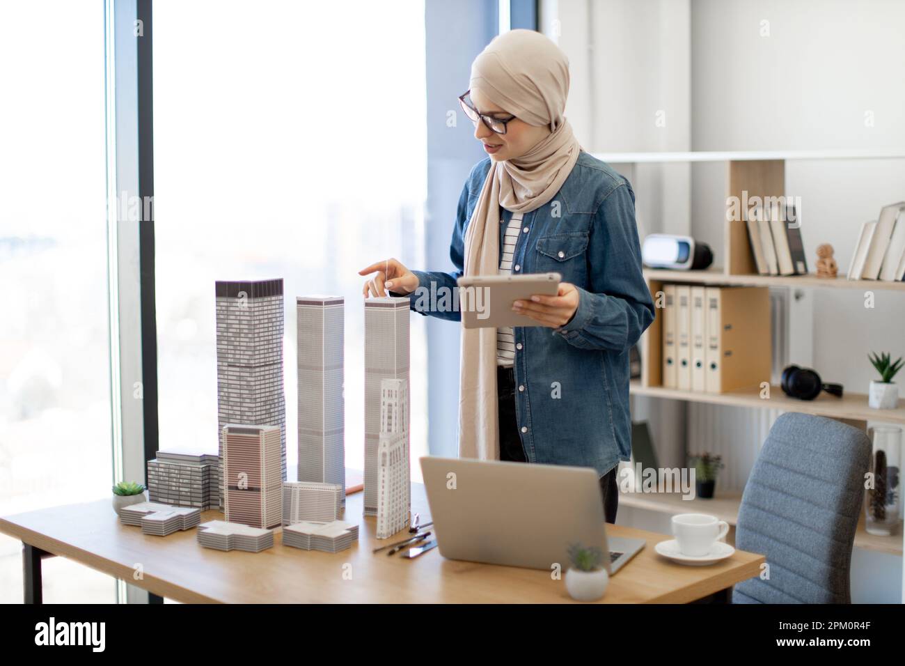 Joyful muslim female in hijab and glasses holding modern tablet while ...