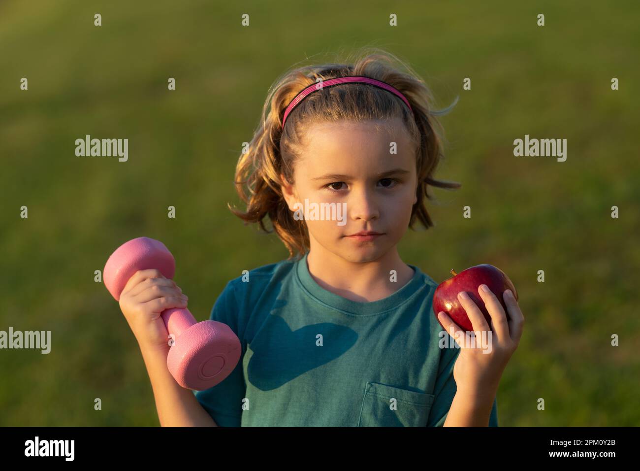 Sporty kid with apple and dumbbell outdoor in summer park. Child boy ...