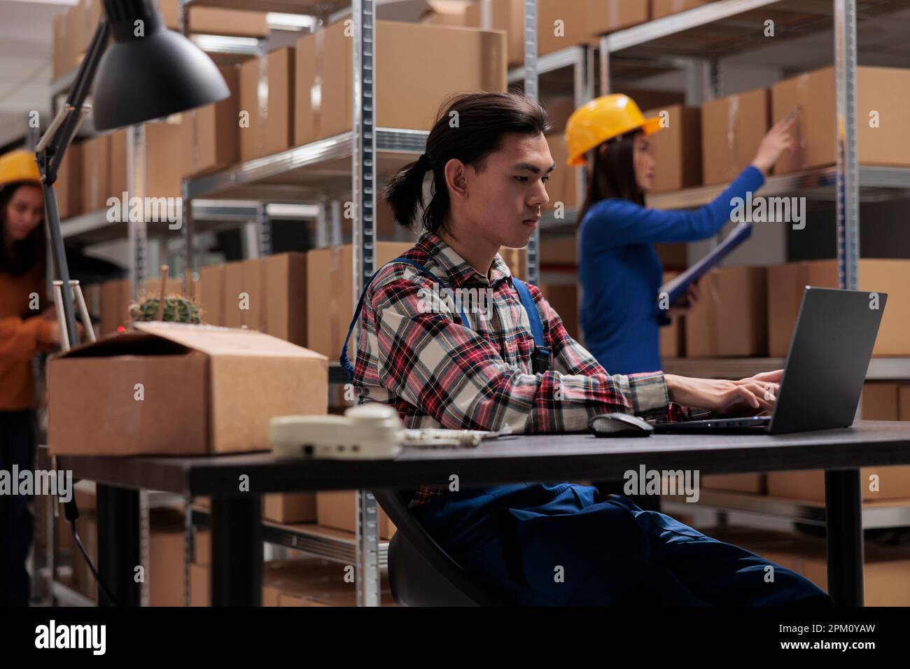 Young asian warehouse supervisor using laptop in storage room ...
