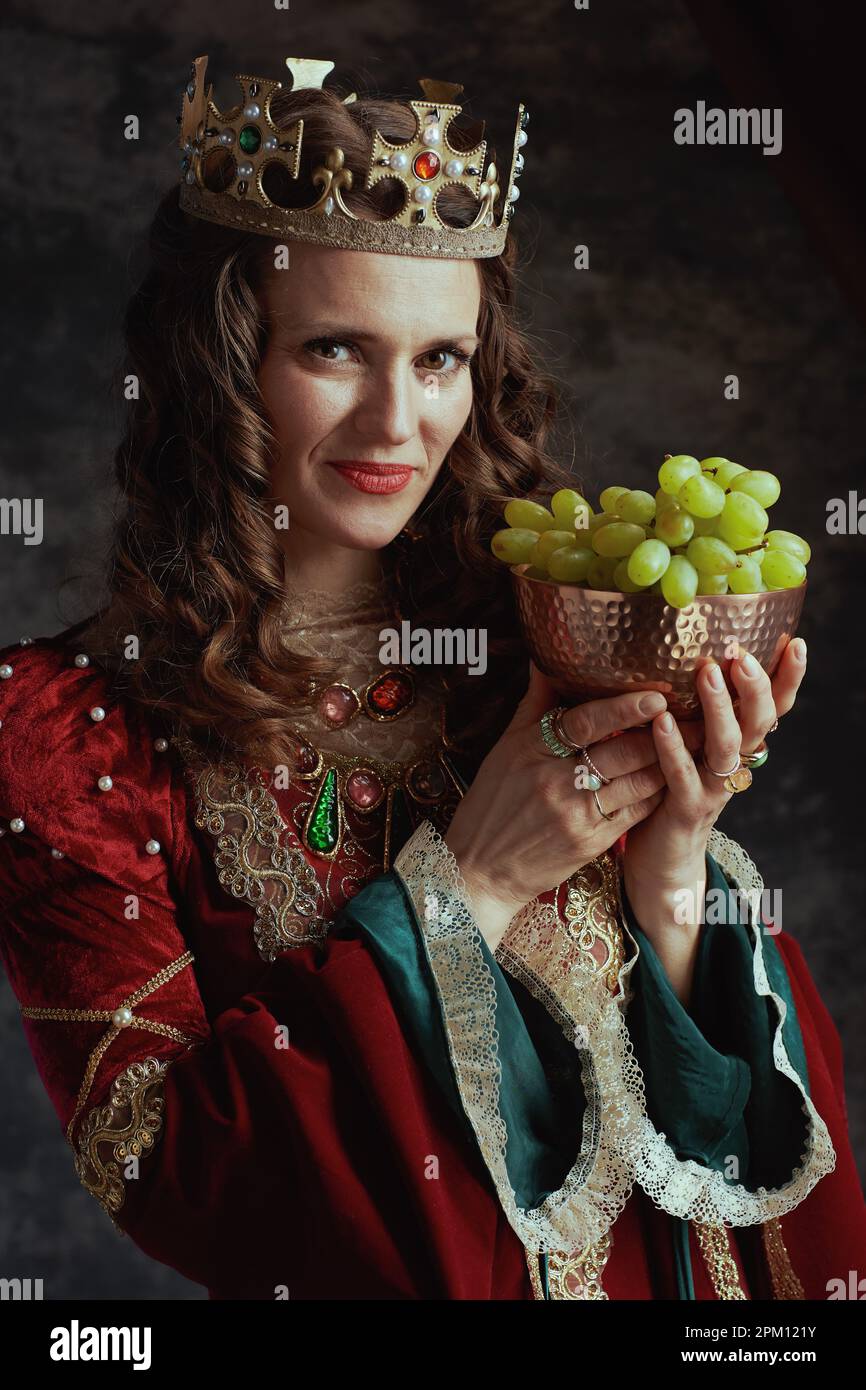 happy medieval queen in red dress with plate of grapes and crown on ...