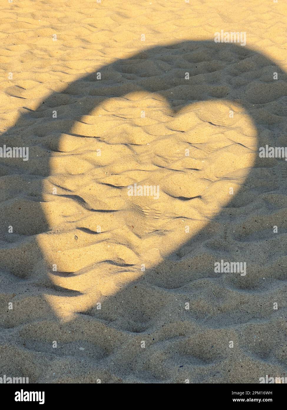 Leftover projection of heart-shaped shadow of structure on beach sand ...