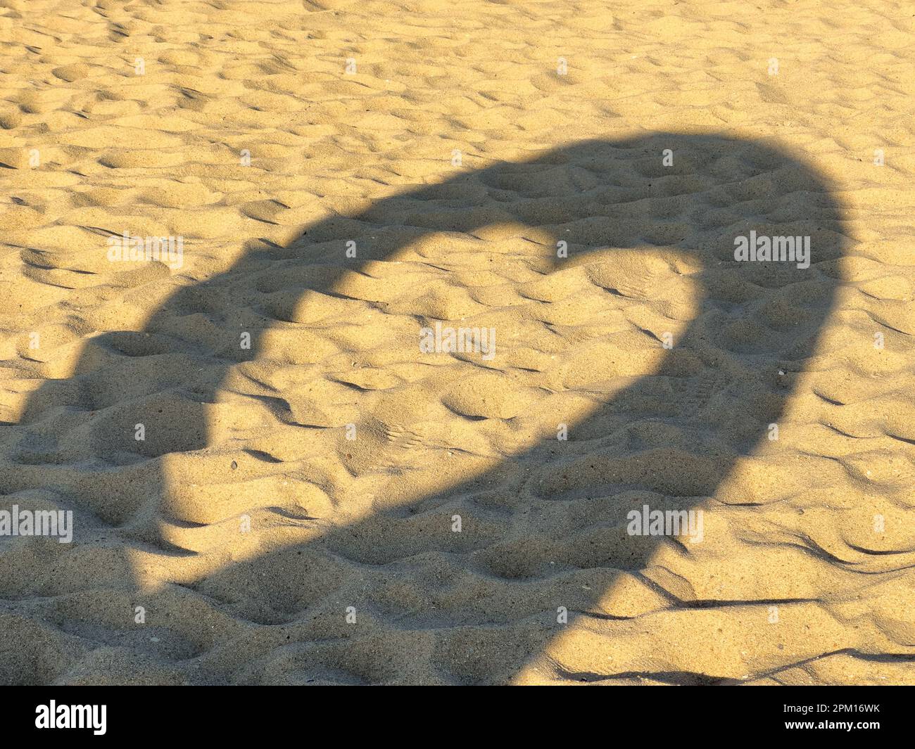 Leftover projection of heart-shaped shadow of structure on beach sand ...