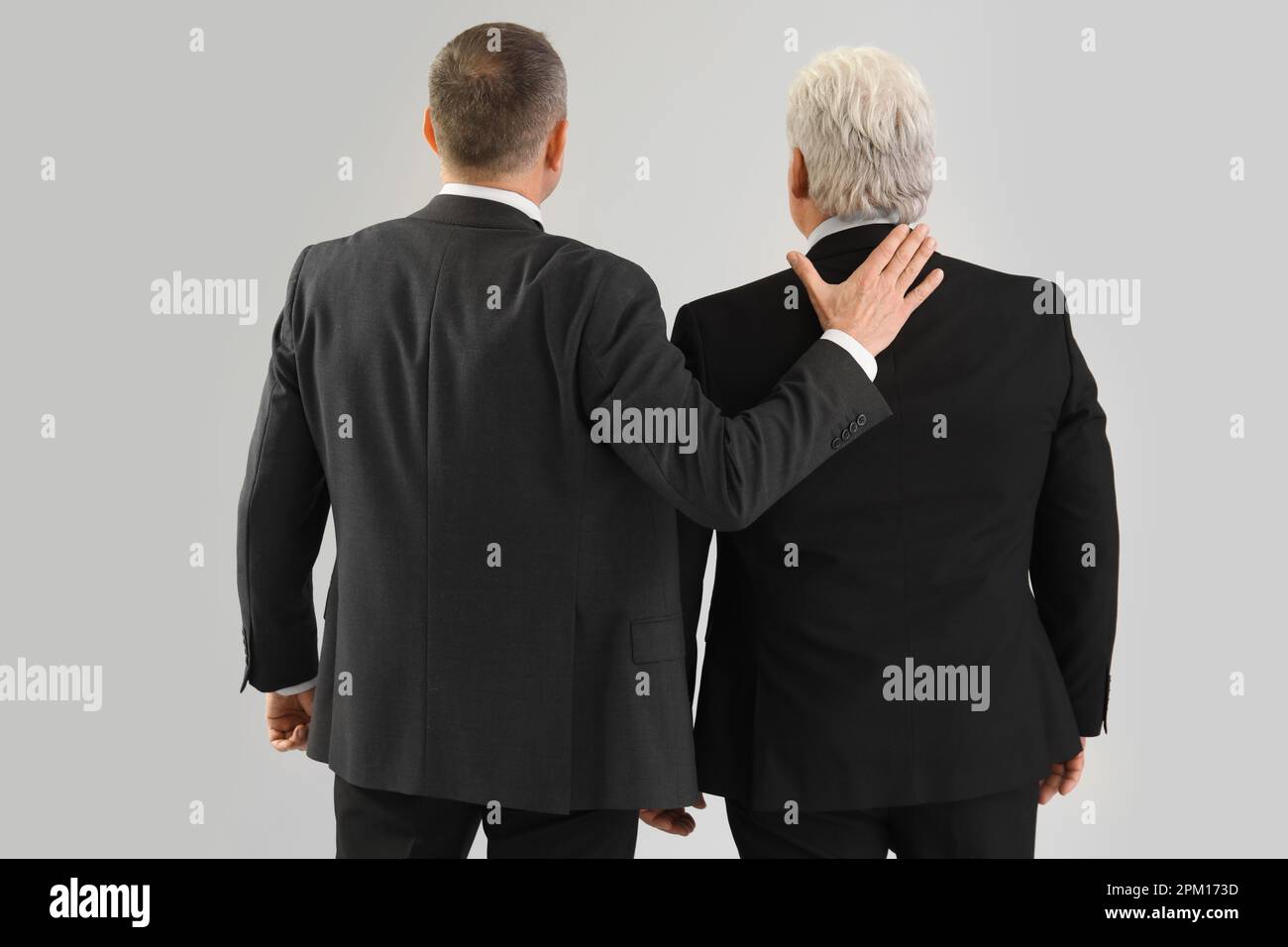 Mature brothers in suits on grey background, back view Stock Photo - Alamy