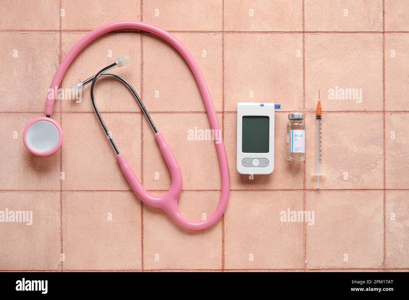 Glucometer with insulin, syringe and stethoscope on pink tile ...