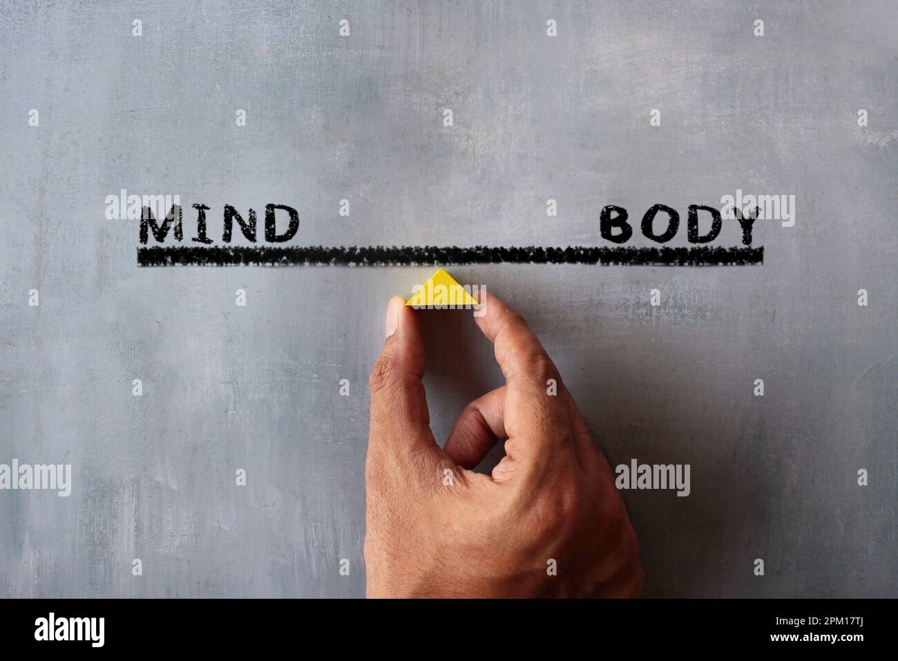 Hand holding wooden triangle with text MIND and BODY on balancing scale ...