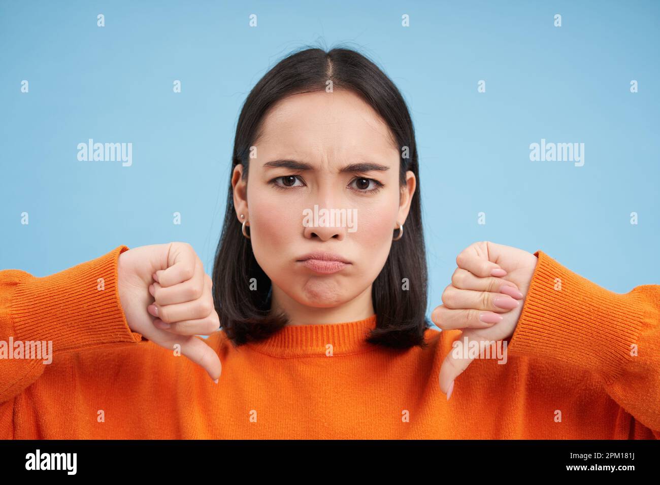 Close up of upset girl shows thumbs down with disappointed face, blue ...