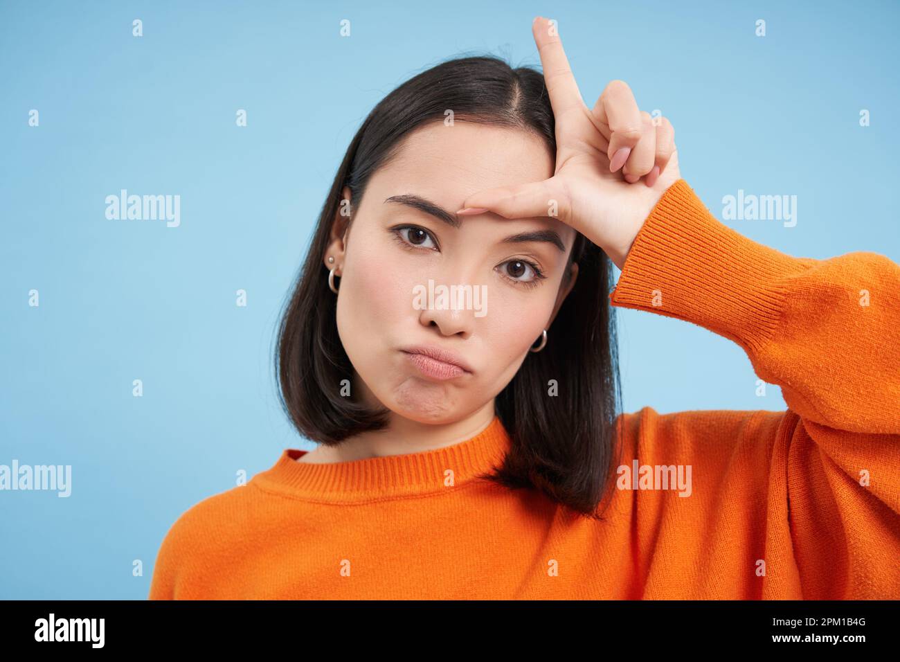 Close up of sassy korean girl, shows letter L, loser symbol on forehead ...