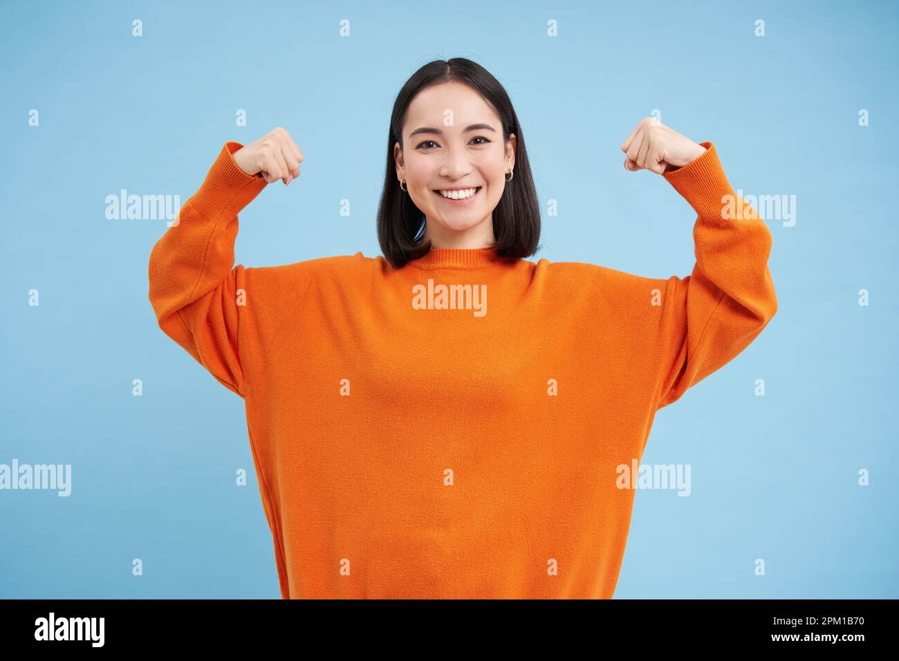 Portrait of cute korean woman flexing her biceps, shows strong arms ...