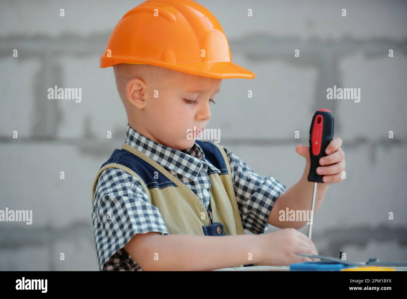 Child play with supplies, tools saw, hammer, screwdriver, helmet ...