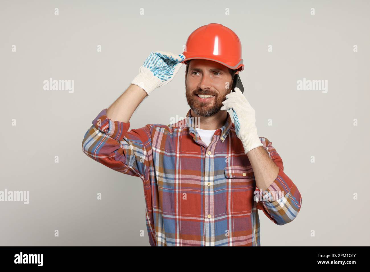 Professional builder in hard hat talking on phone against light ...