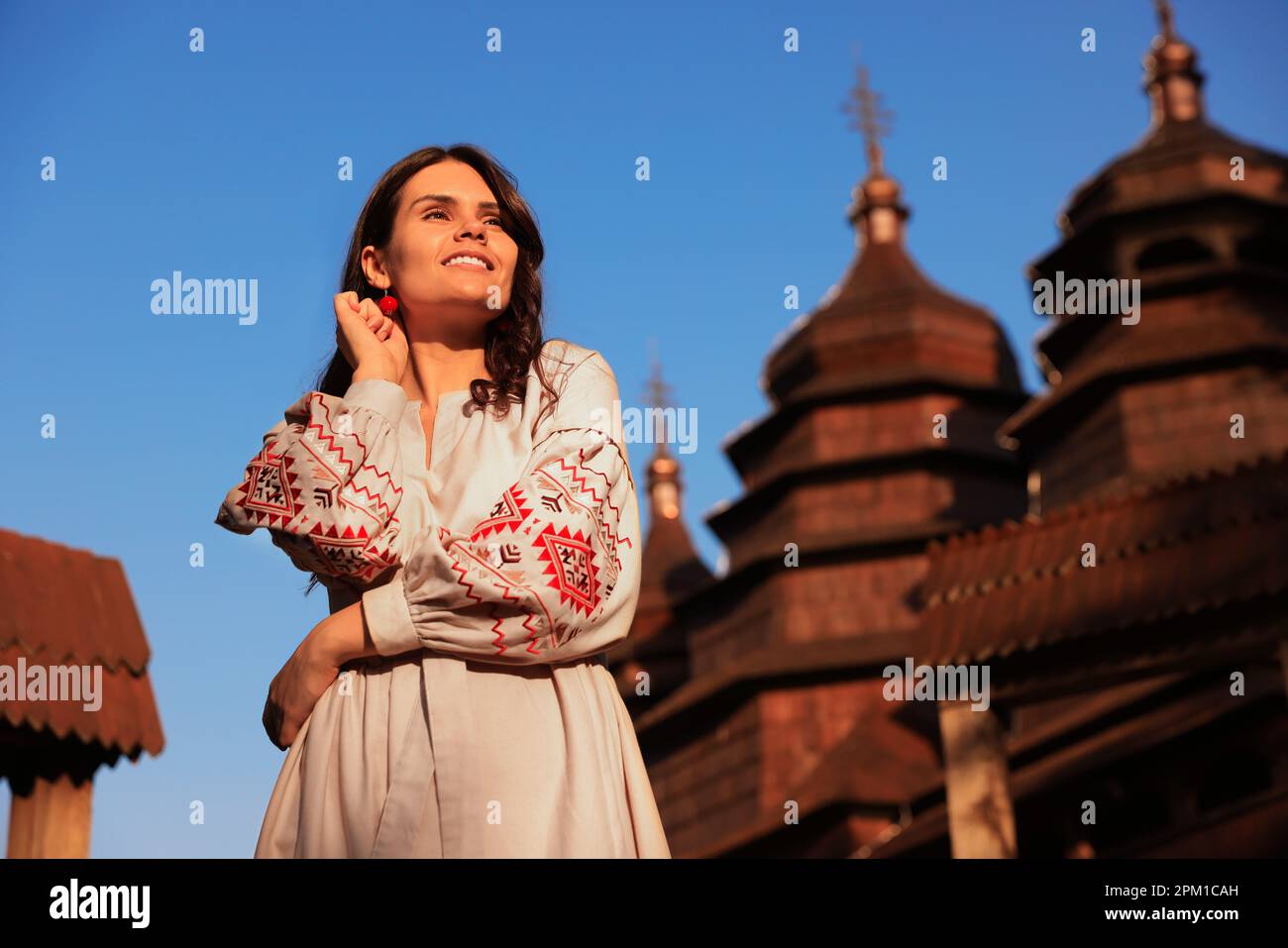 Beautiful woman wearing embroidered dress near old wooden church in ...