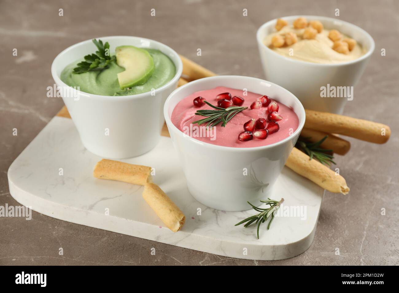 Different delicious hummuses with bread sticks on brown marble table ...