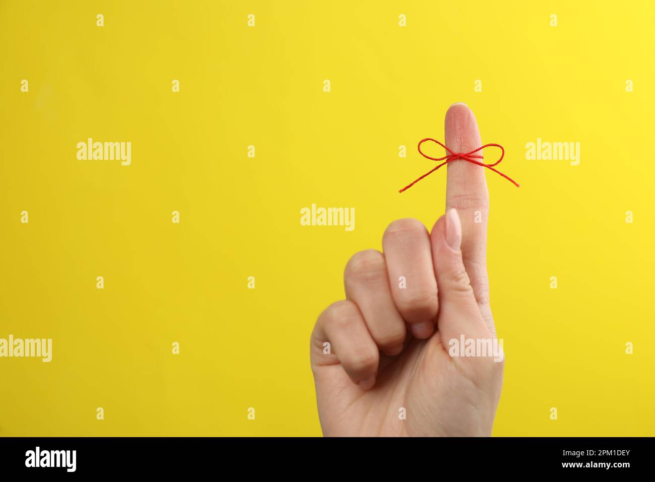 Woman showing index finger with tied red bow as reminder on yellow ...