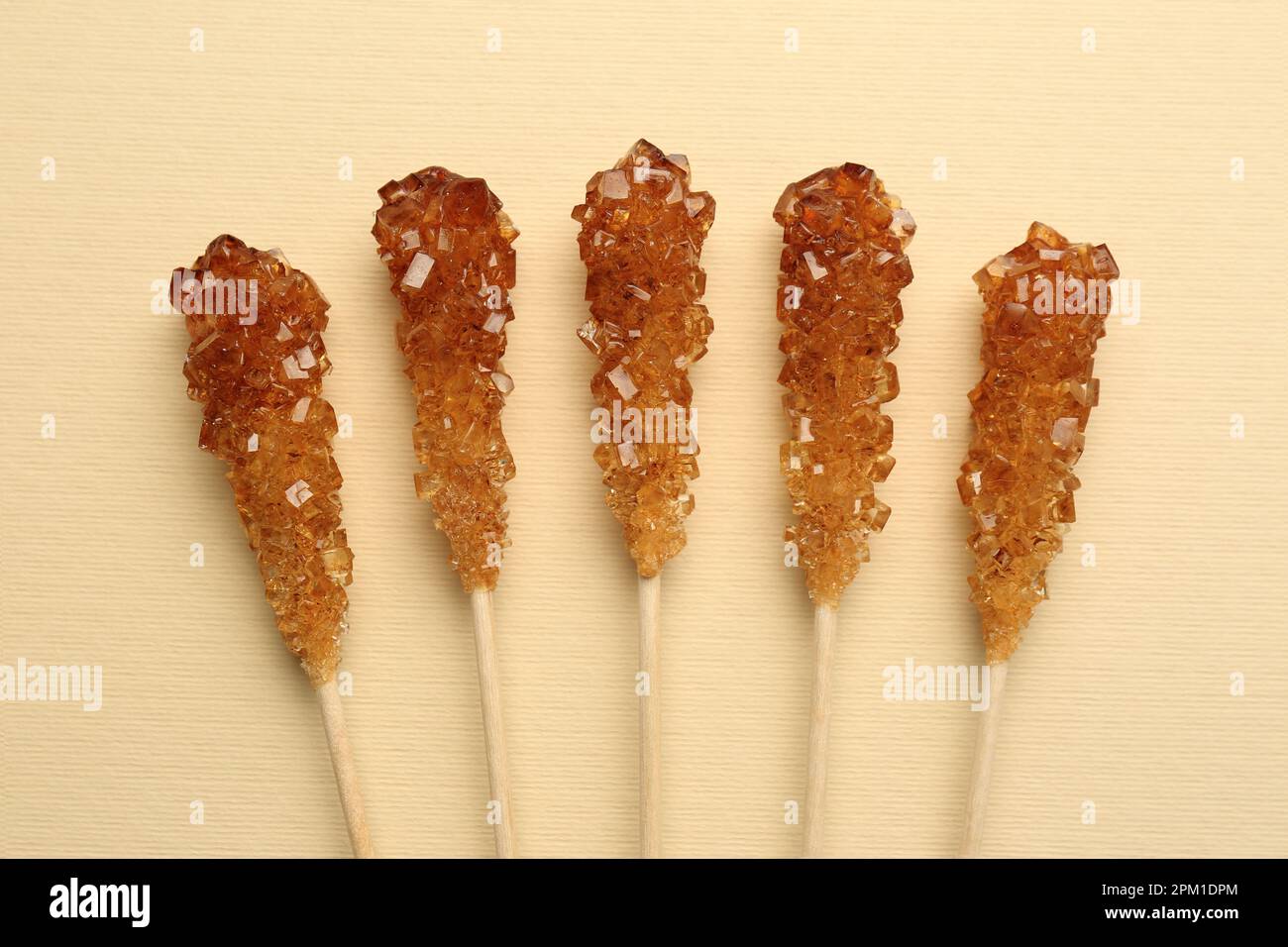Wooden sticks with sugar crystals on beige background, flat lay. Tasty ...