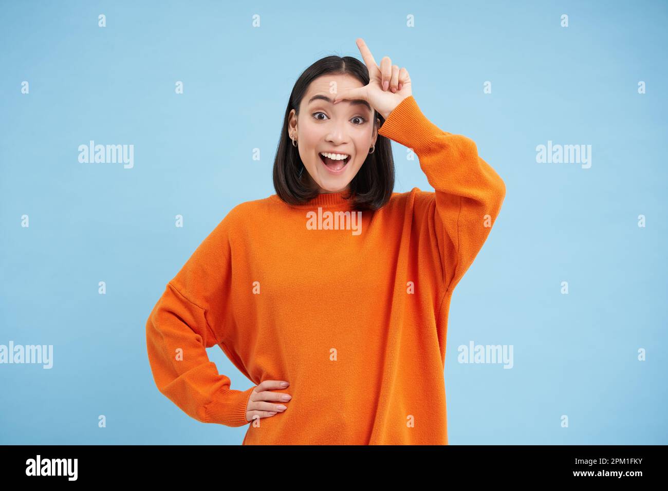 Enthusiastic korean girl, shows L letter on forehead and laughs, mocks ...