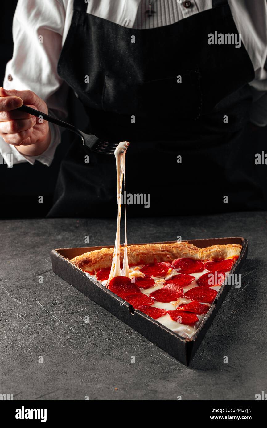 Pulling cheese from slice of pepperoni pizza Stock Photo - Alamy