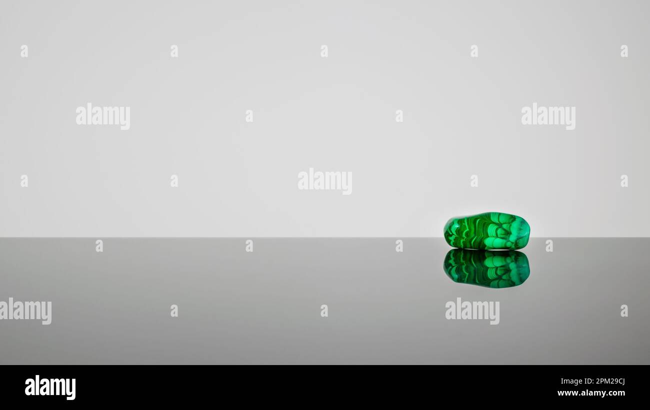 A polished jade rock with its reflection against a grey background ...