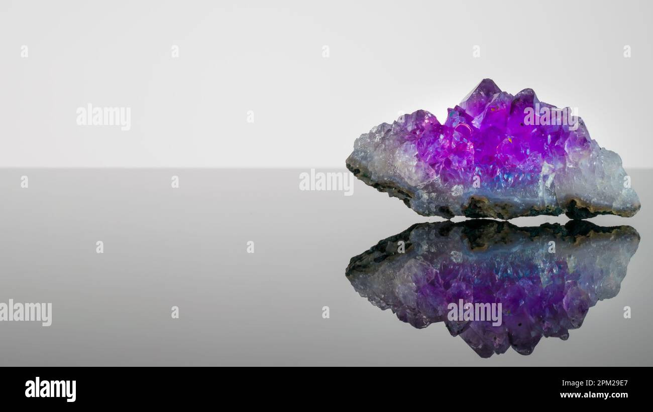 A purple geode rock crystal with its reflection against a grey ...
