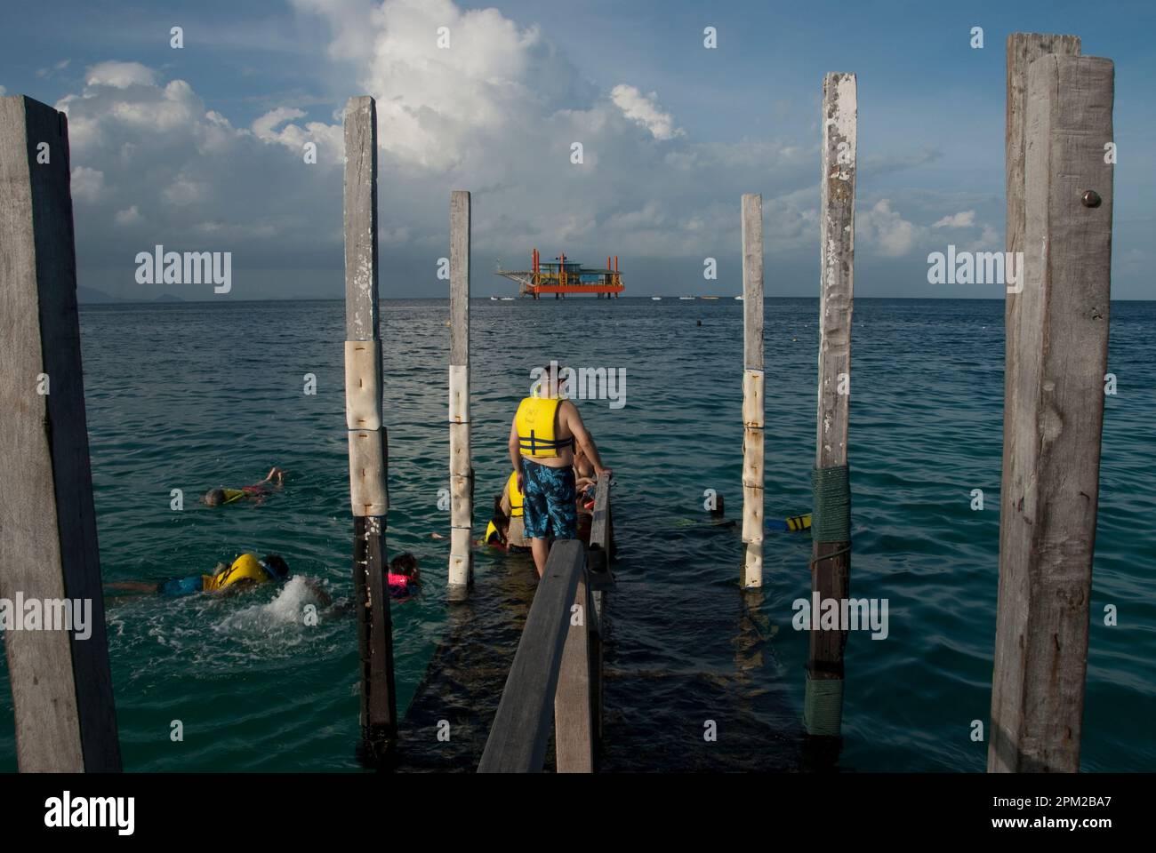 Man on jetty wearing life jacket about to get into water to join other ...