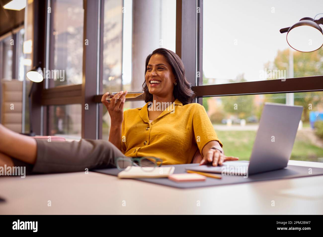 Mature Businesswoman With Feet On Desk Working On Laptop In Office ...