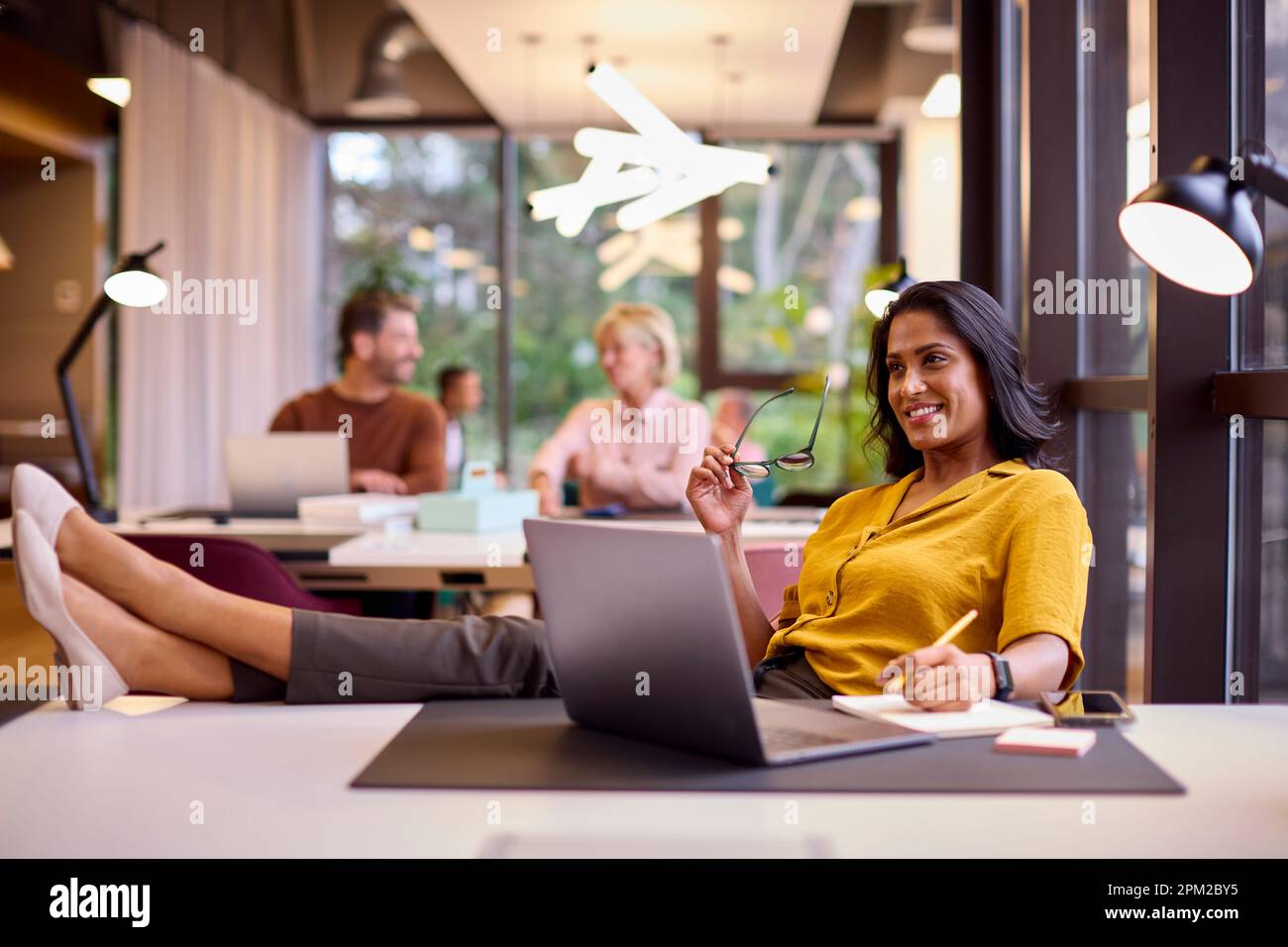Mature Businesswoman With Feet On Desk Working On Laptop In Office ...