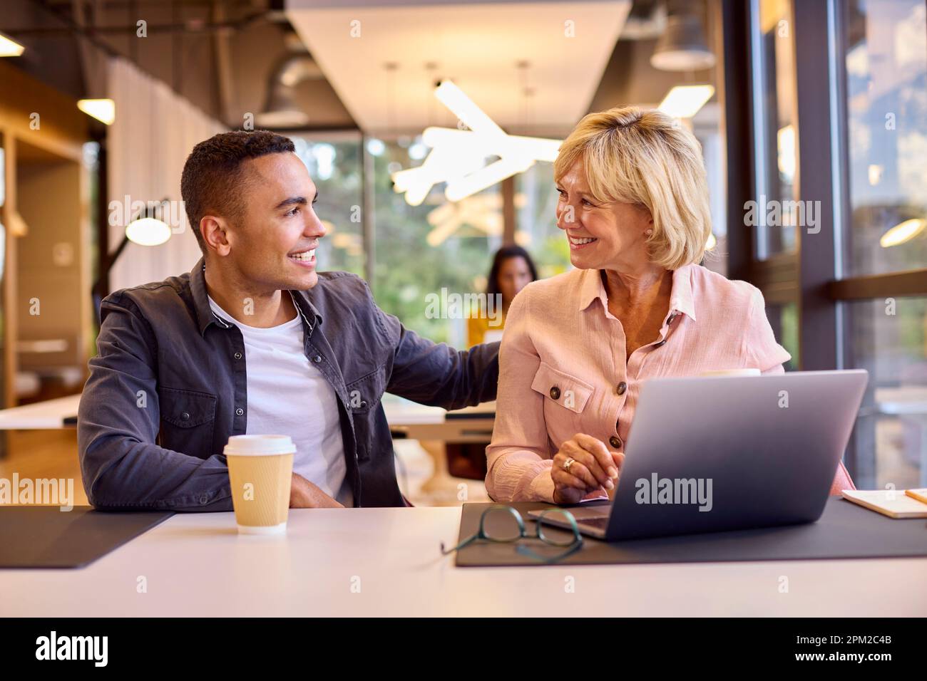 Mature Businesswoman Mentoring Younger Male Colleague Working On Laptop ...