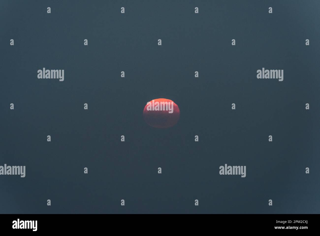 A red full moon rises above the horizon, its shape distorted by the ...