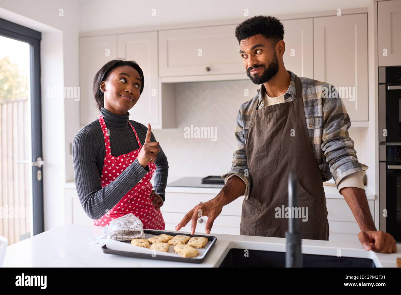 Couple At Home With Man Stealing Homemade Cookie From Tray In Kitchen ...