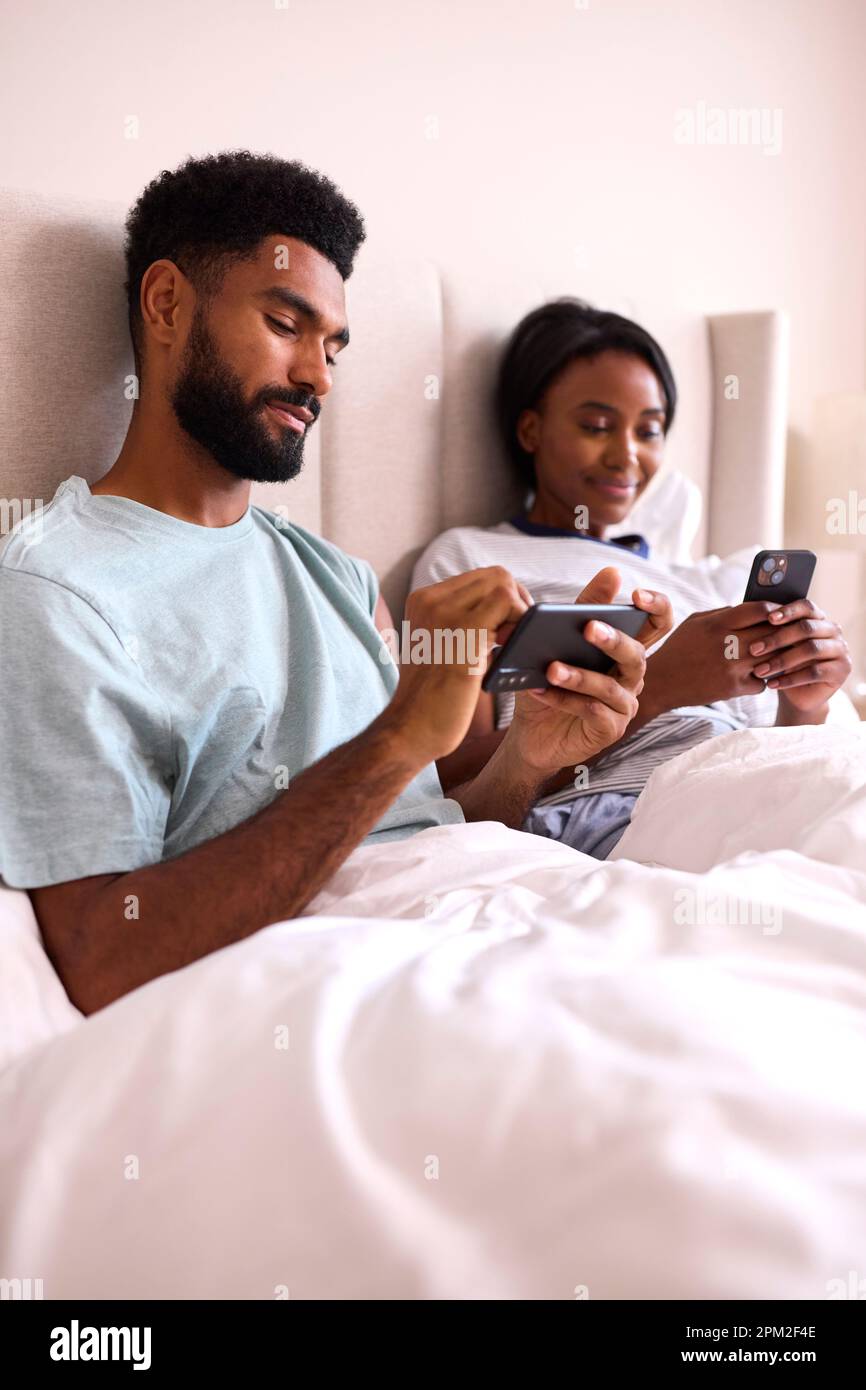Young Couple At Home Both Looking At Mobile Phones In Bed Together ...