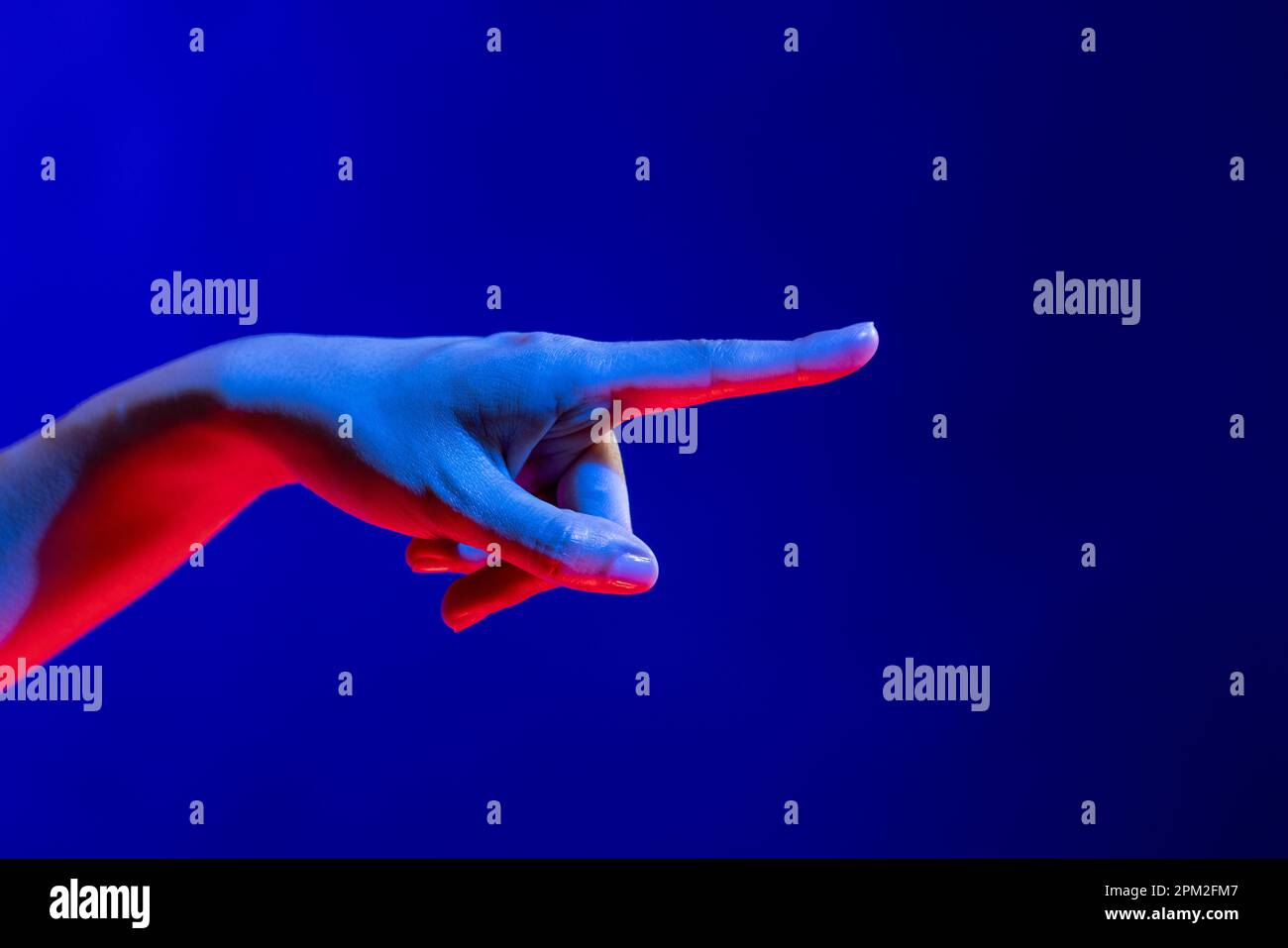 Exposed hand pointing finger in studio with blue light with copy space ...